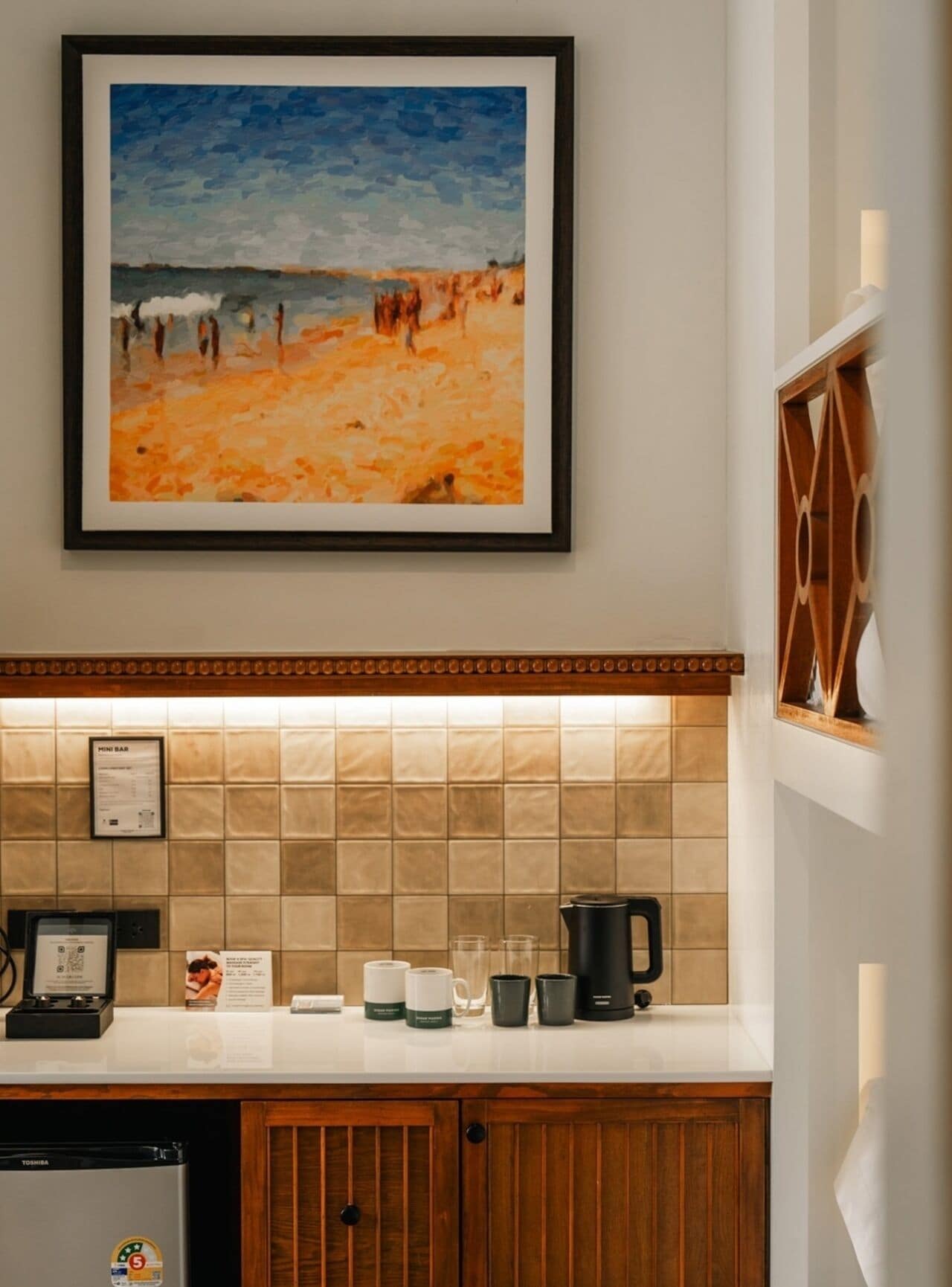 Uma cozinha com painel de azulejos, um quadro emoldurado, placa de minibar e uma cafeteira.