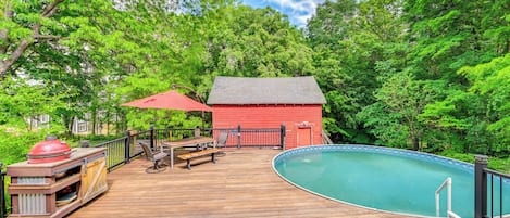 Um deck de madeira com piscina, um edifício vermelho e uma área de churrasco.