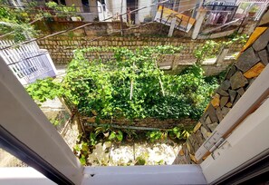 Um pátio estreito com paredes de pedra, plantas em vasos e cerca de metal.