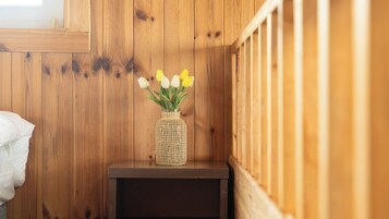Parede de madeira com um vaso trançado contendo flores amarelas e brancas sobre uma pequena mesa de cabeceira de madeira.