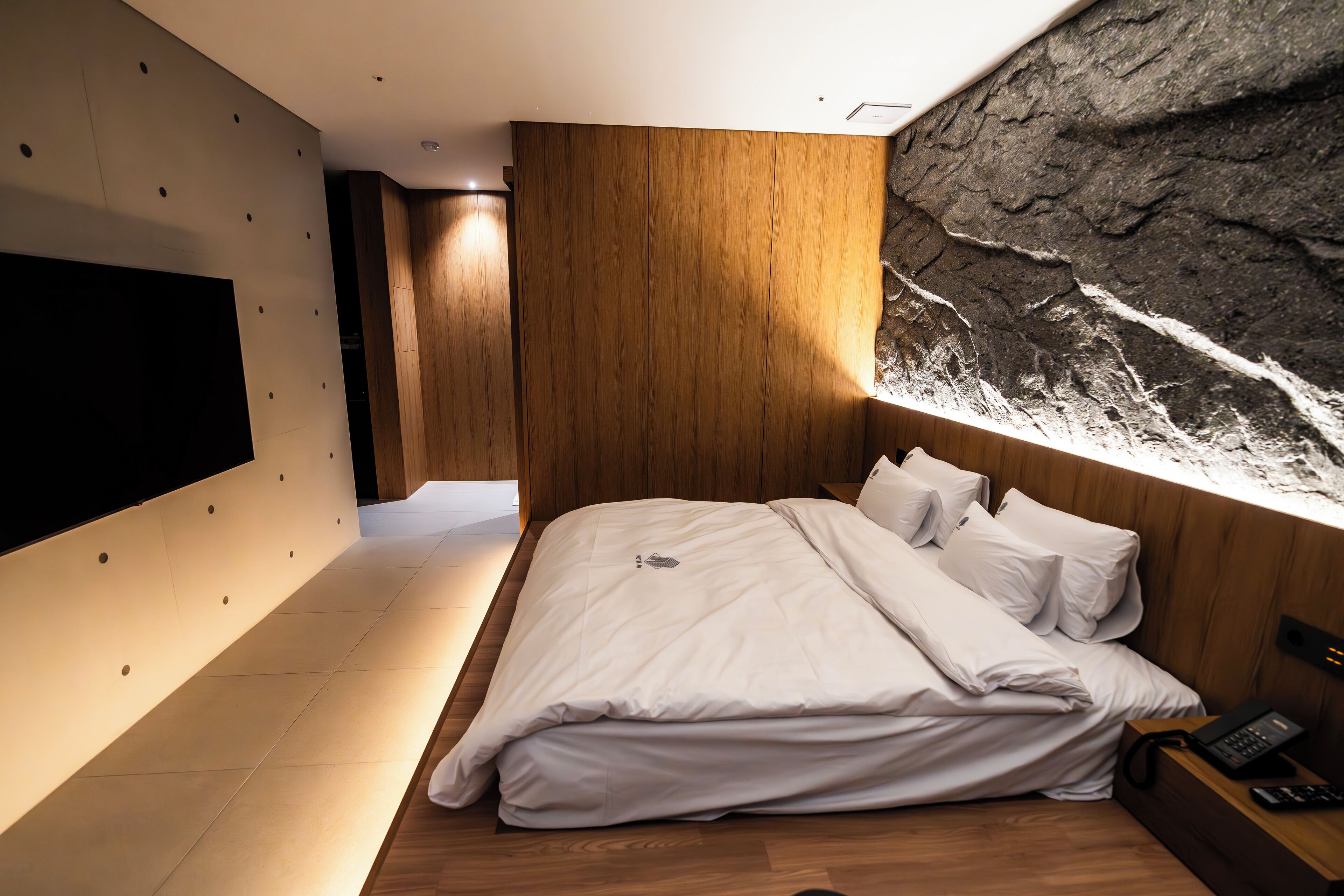 Quarto moderno com cabeceira de madeira, televisão de tela plana na parede e cama com roupa de cama branca.