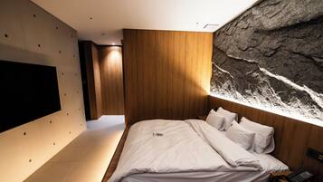 Quarto moderno com cabeceira de madeira, televisão de tela plana na parede e cama com roupa de cama branca.