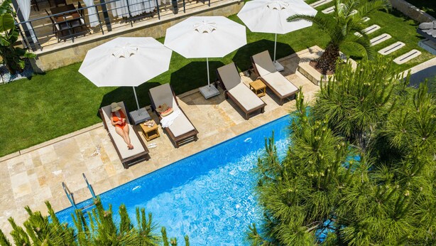 Piscina com espreguiçadeiras e guarda-sóis, cercada por vegetação.