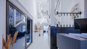 Uma área de recepção moderna com parede de vidro, balcão de atendimento e escada com luminárias pendentes.