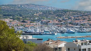 Uma marina com vários barcos atracados, cercada por edifícios residenciais e uma paisagem montanhosa ao fundo.