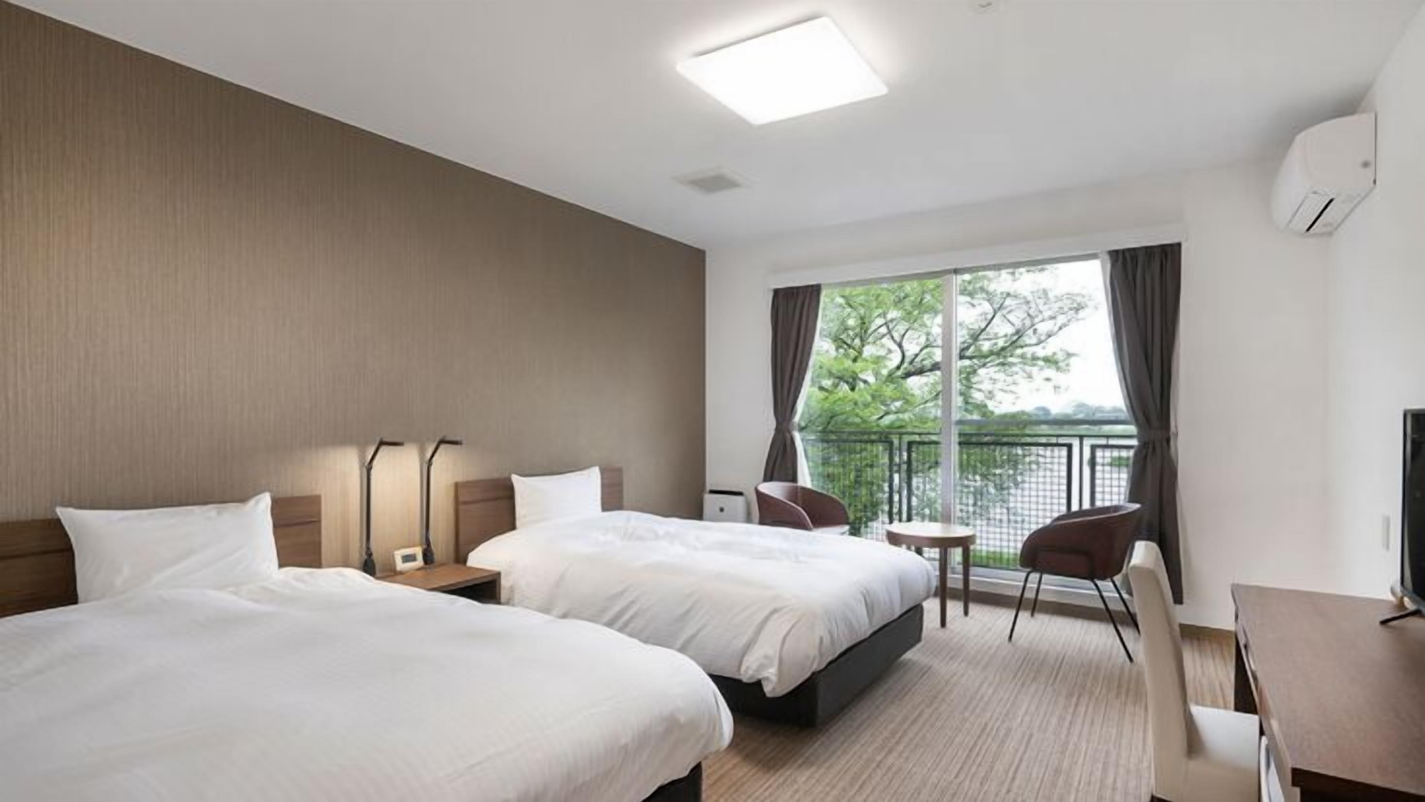 Quarto de hotel com duas camas, uma escrivaninha, uma cadeira, televisão e varanda com vista.