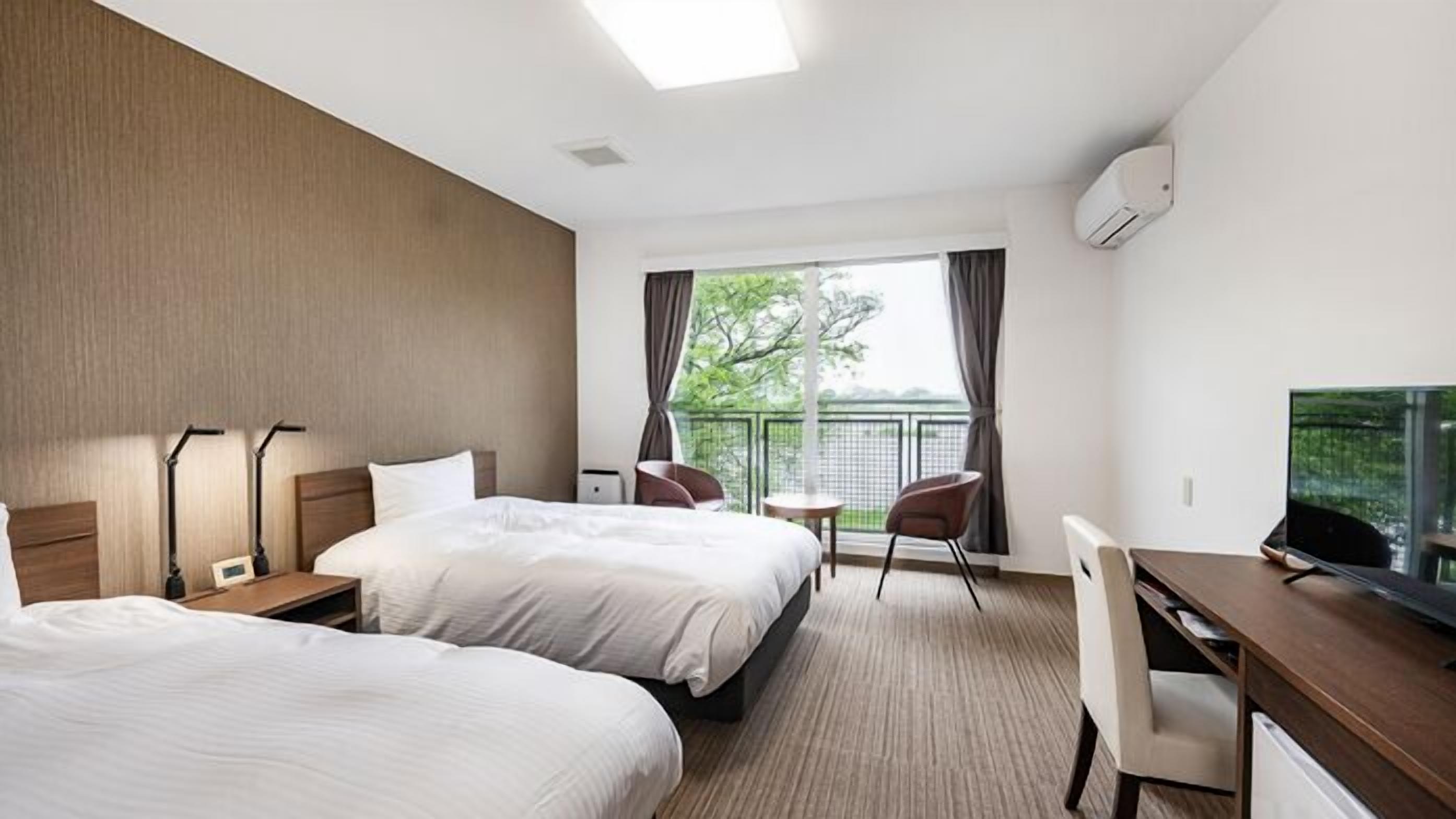 Quarto de hotel com duas camas, uma escrivaninha, uma cadeira, televisão e varanda com vista.