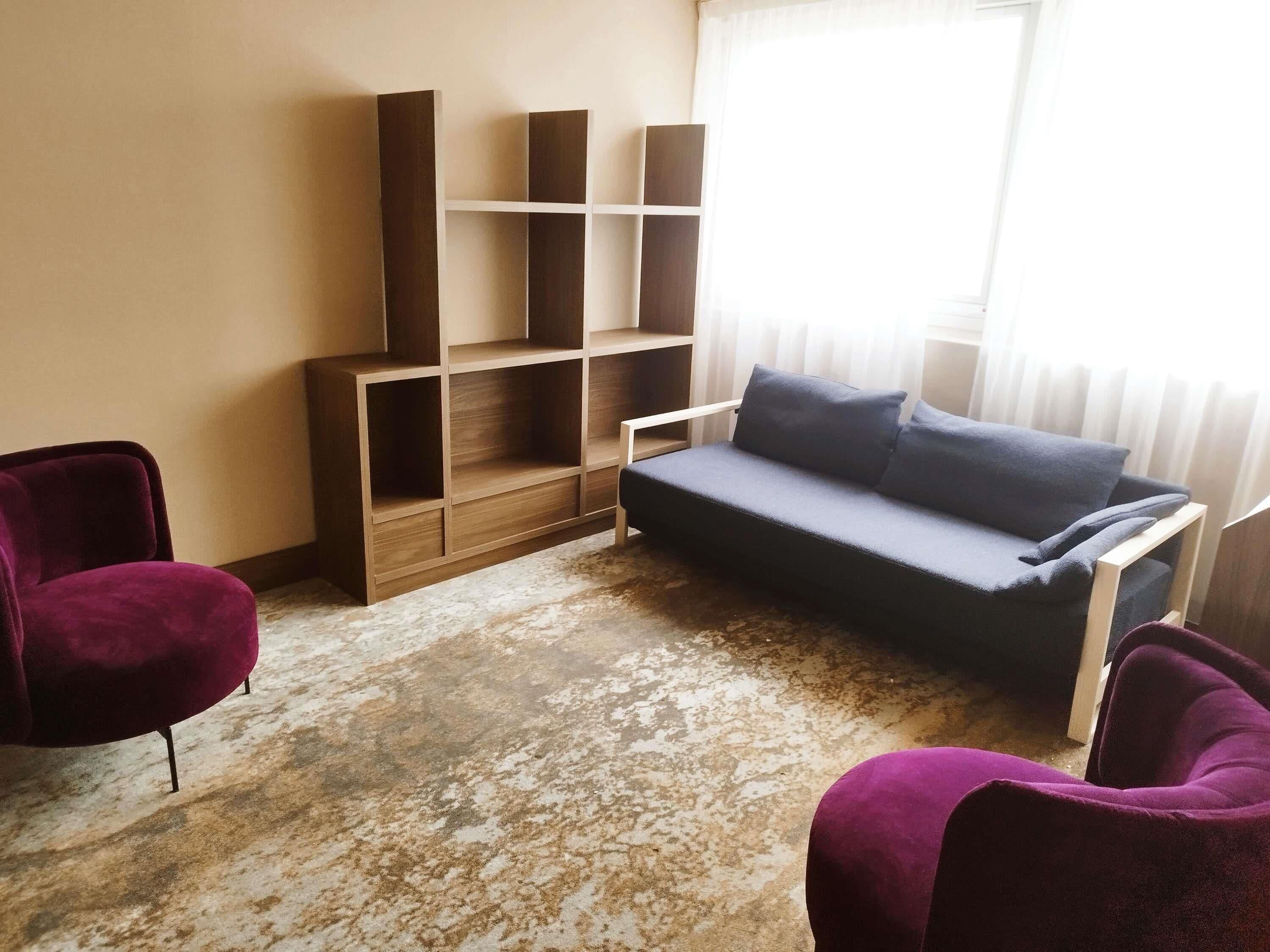 Quarto com sofá, duas cadeiras, estante de madeira e janela com cortinas.