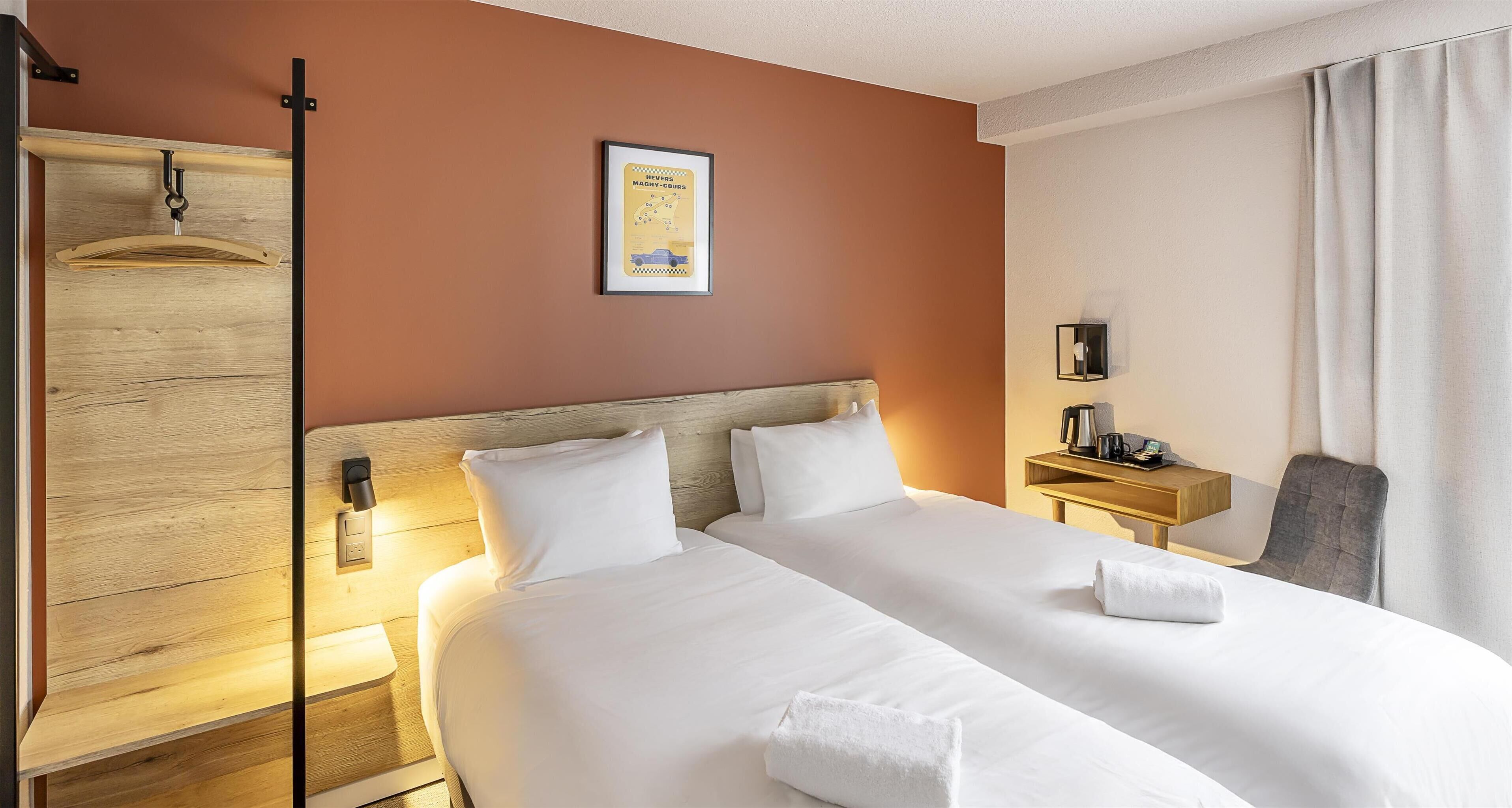 Quarto de hotel com armário de madeira, cama com roupa de cama branca, mapa emoldurado na parede, mesa de cabeceira com abajur e uma cadeira.