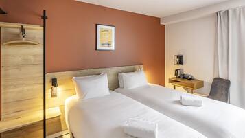 Quarto de hotel com armário de madeira, cama com roupa de cama branca, mapa emoldurado na parede, mesa de cabeceira com abajur e uma cadeira.