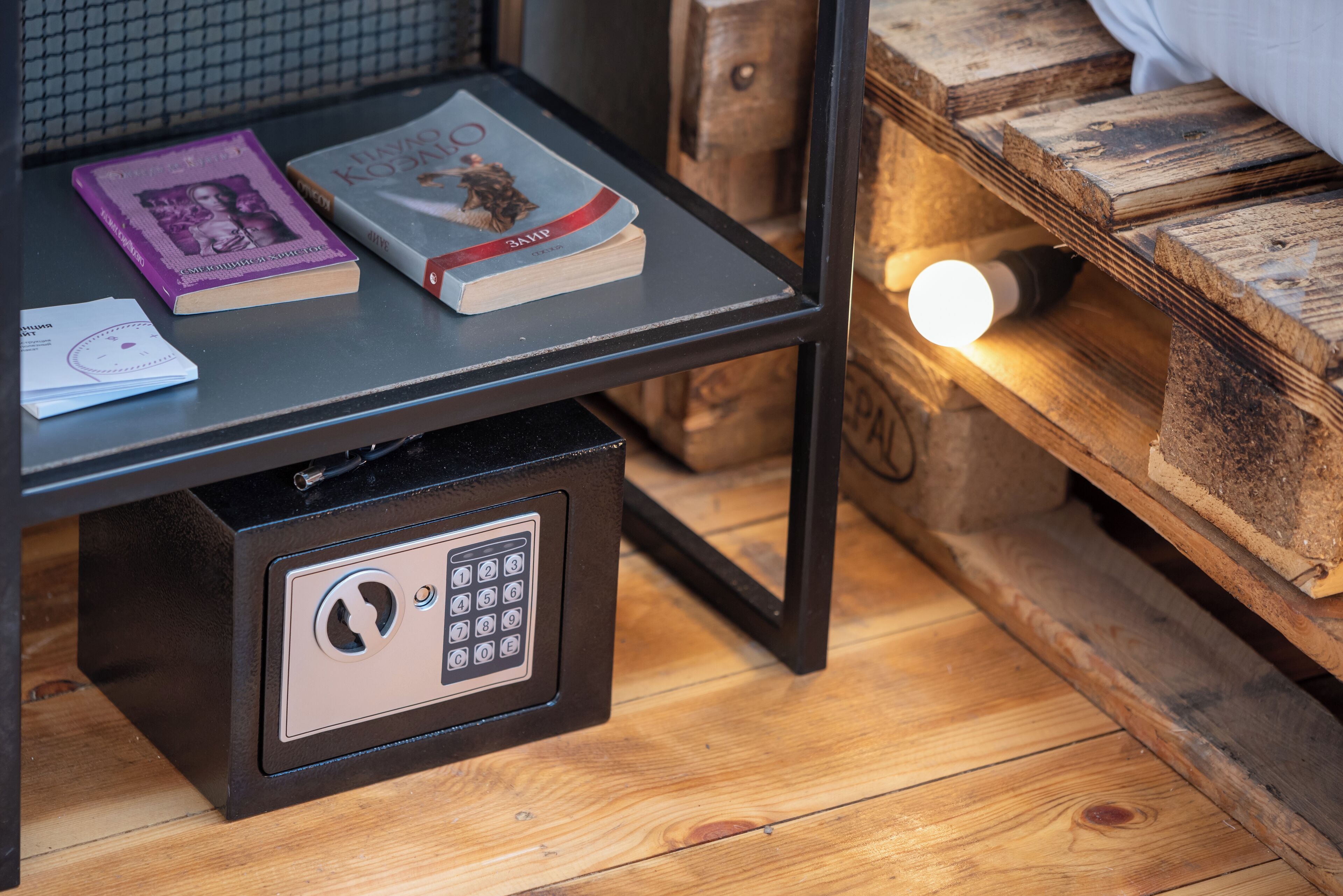 Piso de madeira, uma mesa de metal com livros e um cofre.