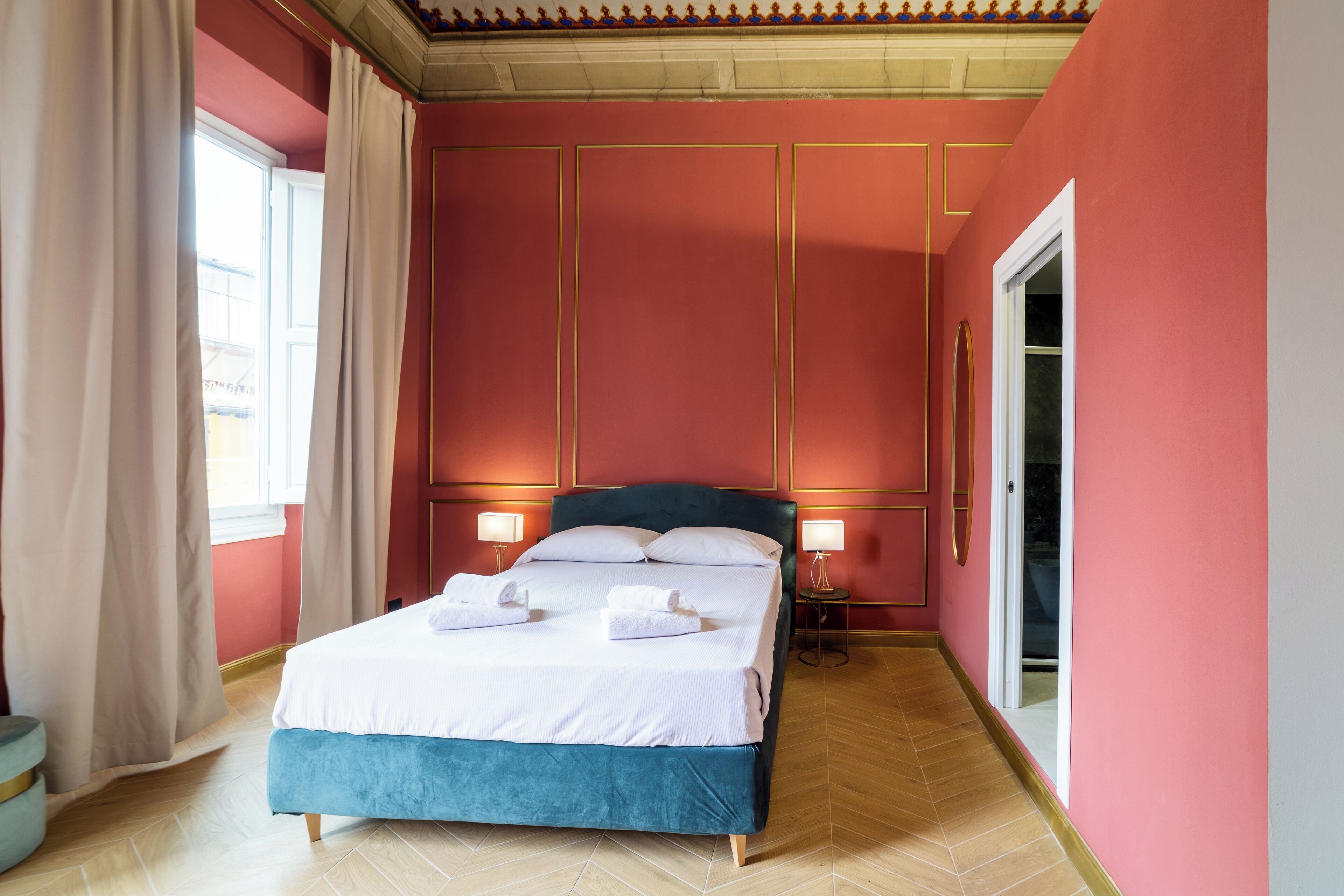 Quarto com cama, duas luminárias de cabeceira, janela com cortinas e porta.
