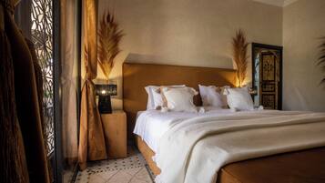 Quarto com cama grande, mesa de cabeceira, luminária e plantas decorativas.