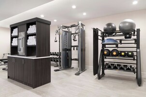 Uma academia com equipamentos de musculação, um suporte de halteres e um espaço para toalhas.