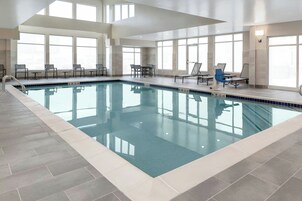 Piscina interna com revestimento de azulejos, várias espreguiçadeiras e janelas amplas que oferecem luz natural.