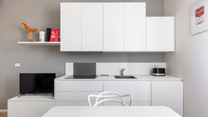 Uma cozinha moderna com armários brancos, uma TV de tela plana, uma cafeteira e um pequeno estante com objetos decorativos.