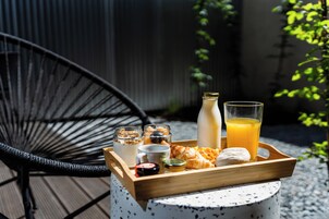 Bandeja de café da manhã com croissants, garrafa de leite, copo de suco de laranja e diversos acompanhamentos em uma mesa ao ar livre.