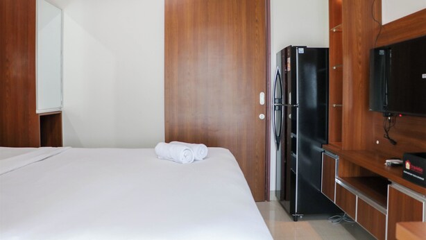 Quarto de hotel com uma cama, um guarda-roupa de madeira, um refrigerador preto e uma televisão.