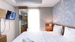 Quarto de hotel com cama, televisão na parede, escrivaninha e uma luminária, e espelho.