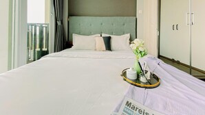 Quarto de hotel com uma cama grande, cabeceira cinza, guarda-roupa e janela com cortinas.