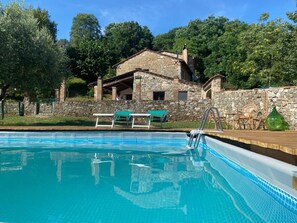 Piscina com espreguiçadeiras e um edifício de pedra ao fundo.