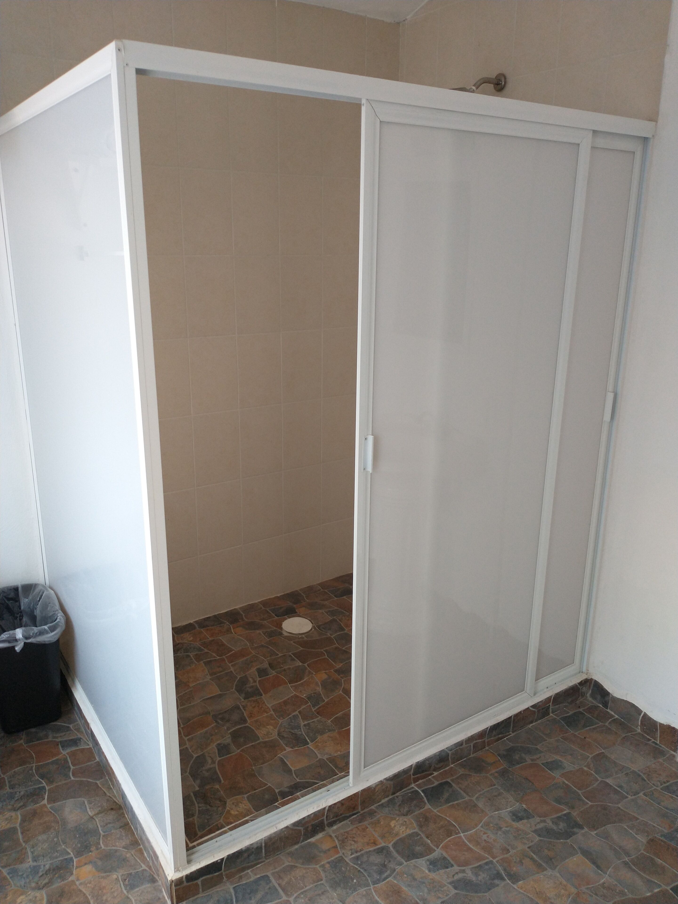 Quarto com guarda-roupa branco, área de chuveiro com azulejos e um cesto de lixo.