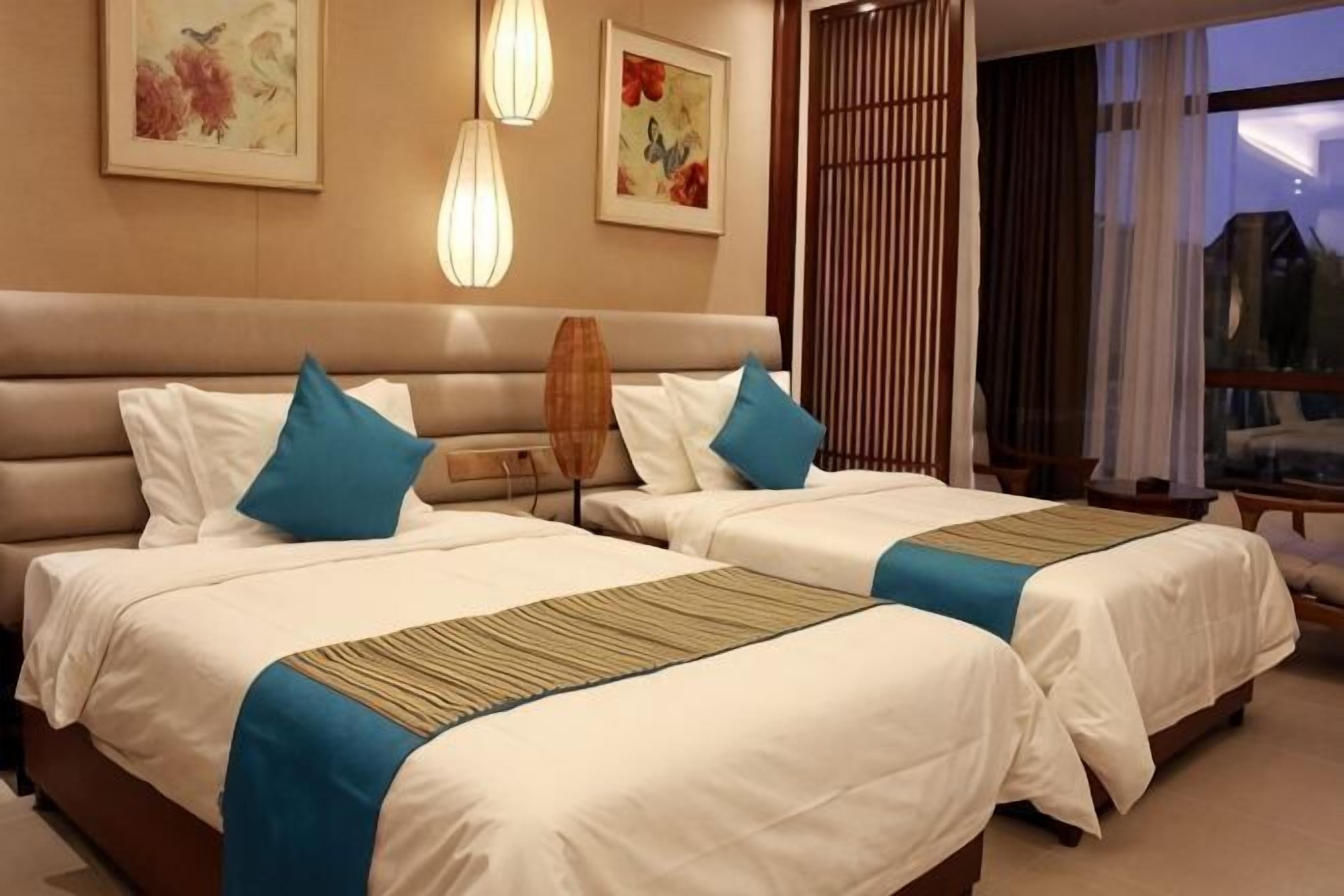 Quarto de hotel com duas camas, uma janela grande e obras de arte nas paredes.