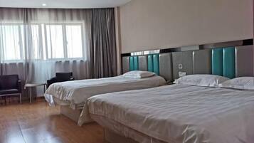 Quarto de hotel com duas camas, uma cadeira, uma mesinha e uma janela com cortinas.