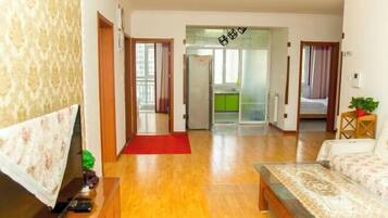 Quarto de hotel com piso de madeira, televisão, sofá, tapete vermelho e porta que dá para outro cômodo.