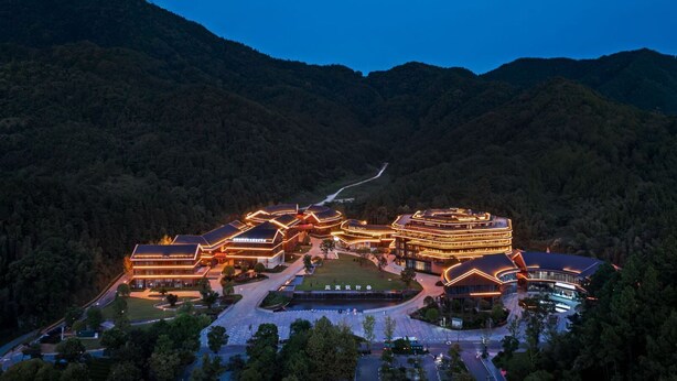 Um hotel grande, de vários andares, com arquitetura tradicional, rodeado por colinas arborizadas.