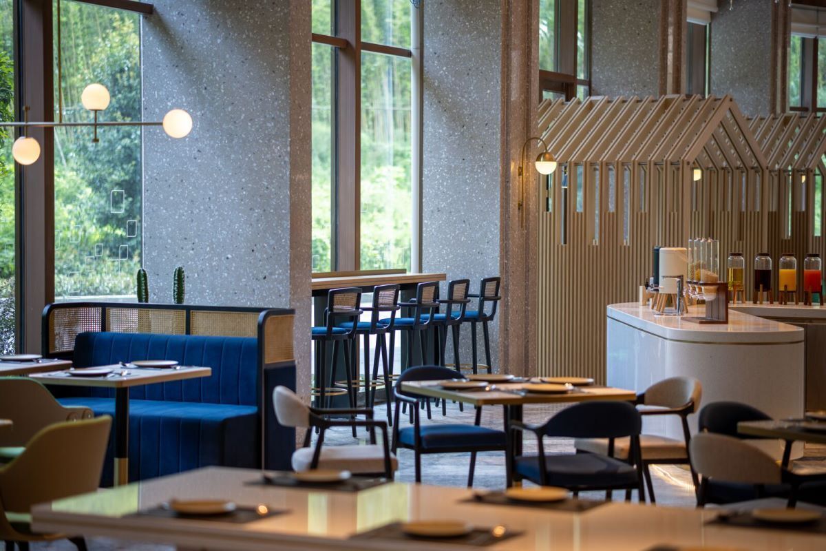 Interior moderno de restaurante com pé direito alto, amplas janelas e diversas opções de assento, incluindo cabines e mesas.