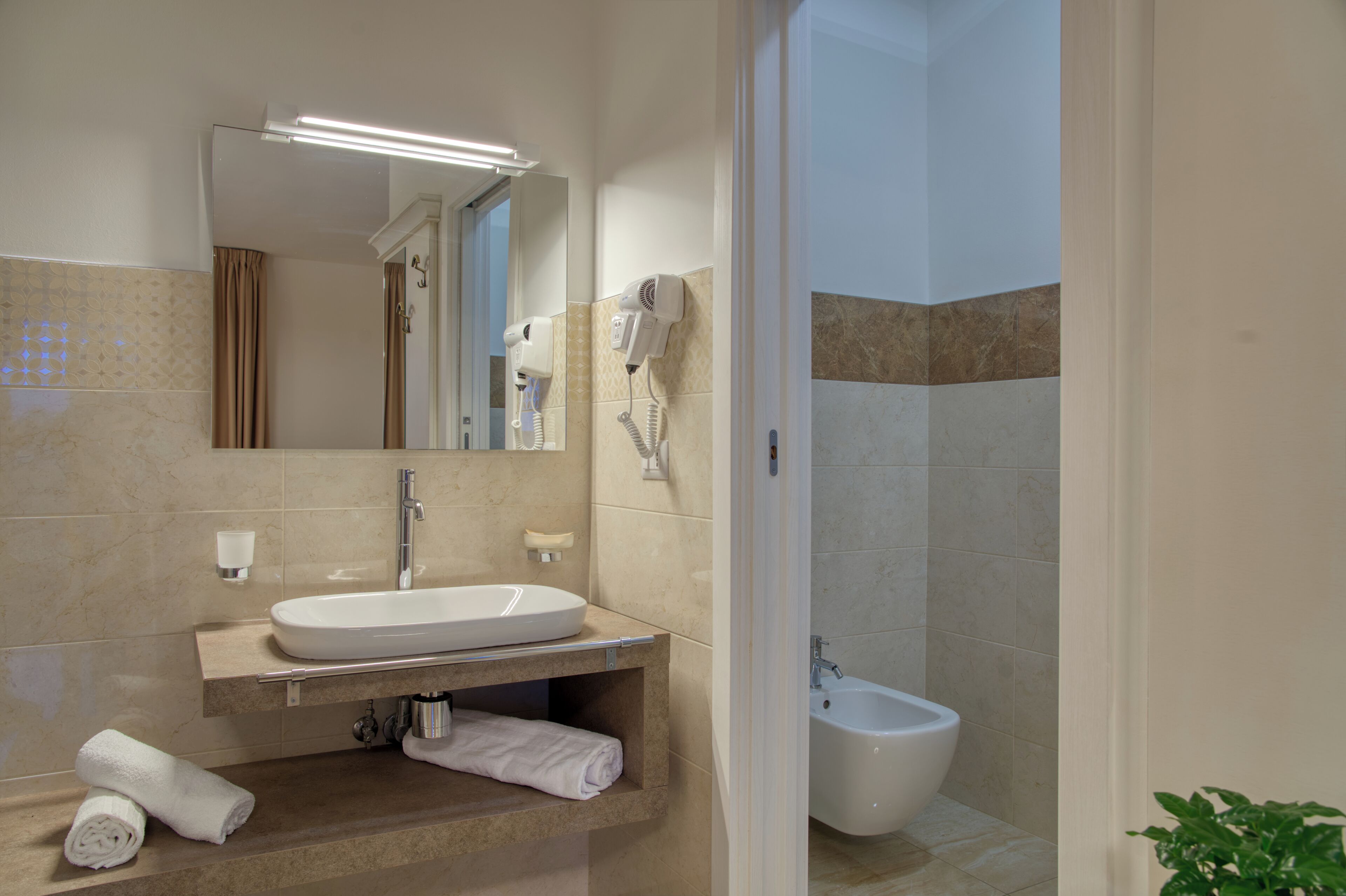 Uma casa de banho moderna com lavatório, espelho, secador de cabelo e bidé.