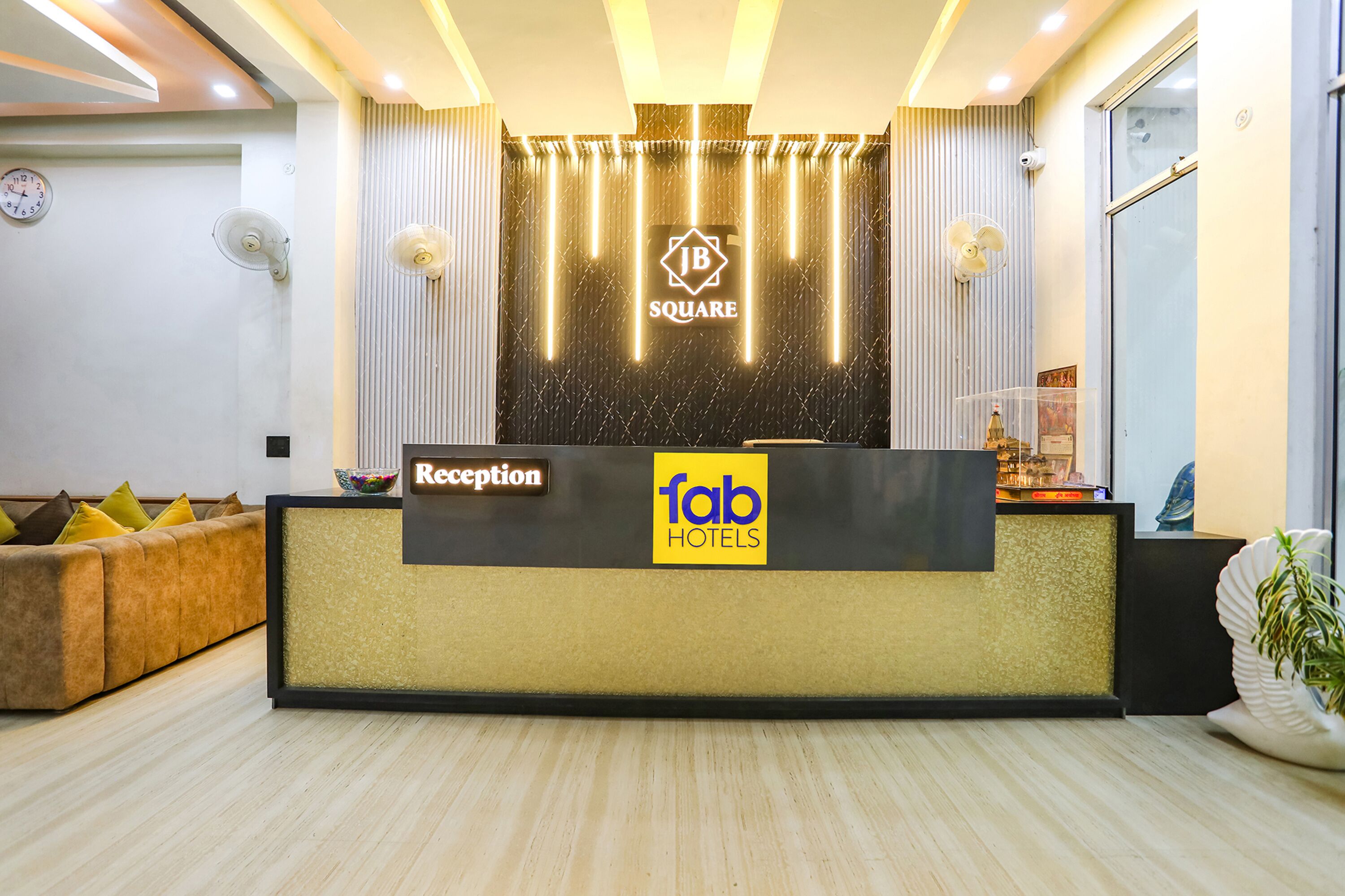 Balcão de recepção com placa 'Reception', logotipo 'JB SQUARE' e placa 'fab HOTELS'.