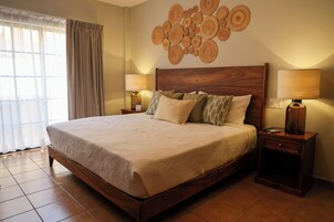 Uma cama bem arrumada com cabeceira de madeira, duas mesas de cabeceira com luminárias e uma obra de arte na parede acima da cama.