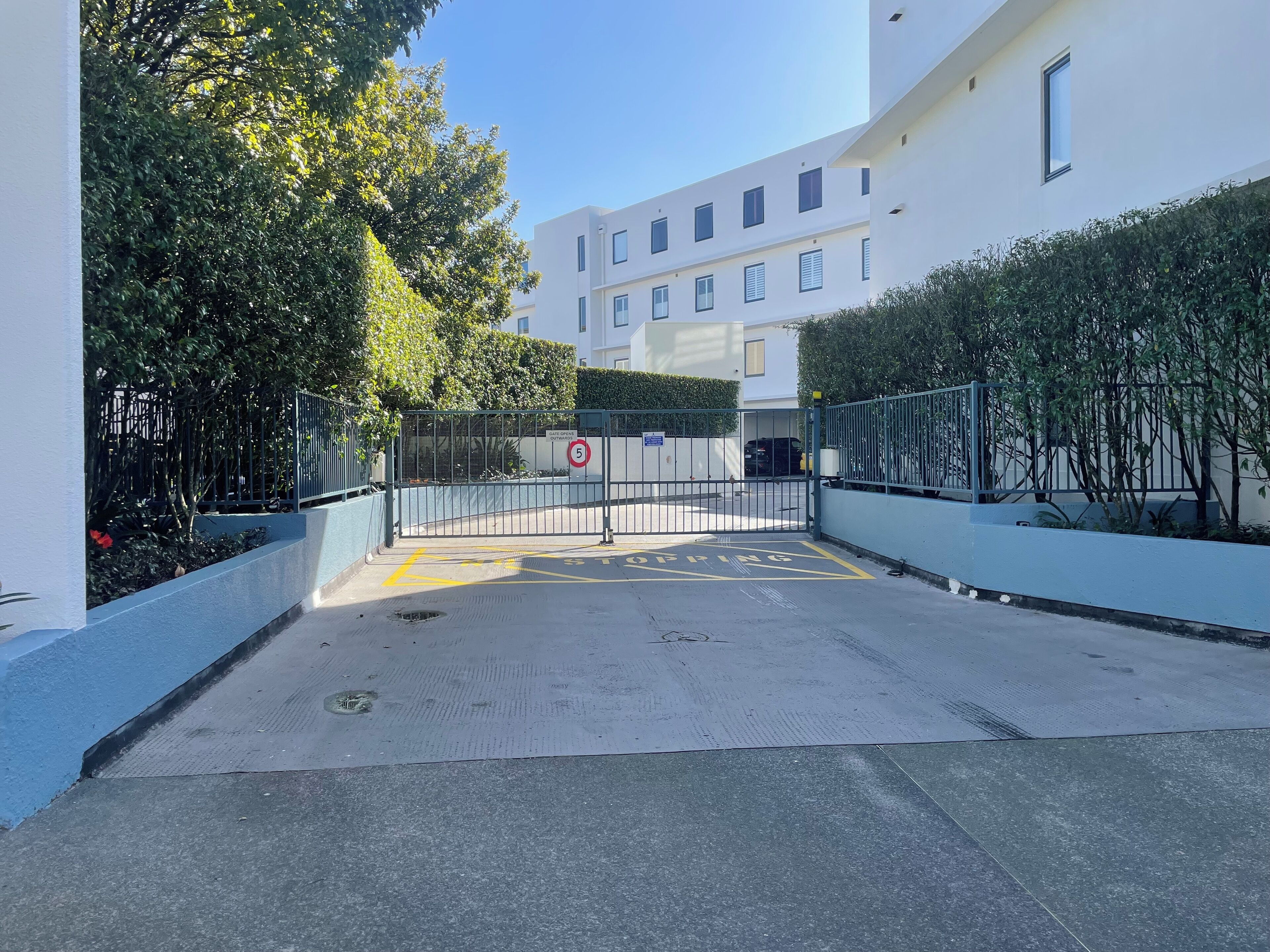Uma área de estacionamento murada com uma estrada bem visível que leva a um edifício com várias janelas.