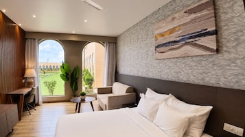 Quarto de hotel com cama, sofá, escrivaninha e vista para um pátio.