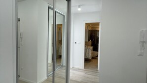 Interior moderno com porta de vidro para um banheiro, piso de madeira e área de cozinha visível.