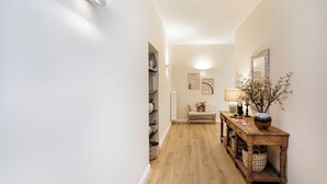 Um corredor com piso de madeira, um aparador com objetos decorativos, um espelho e obras de arte nas paredes.