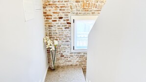 Quarto com parede de tijolos, janela e um vaso com flores brancas.