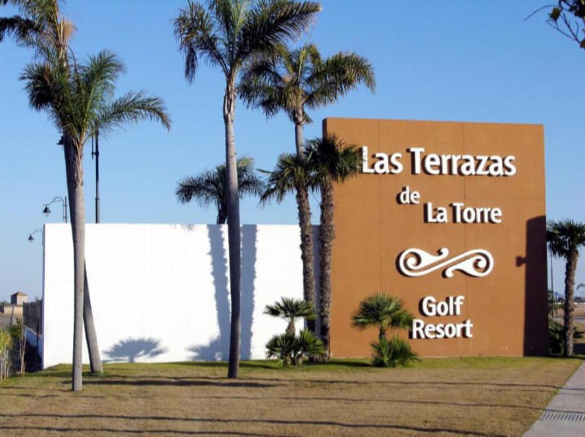 Placa para Las Terrazas de La Torre Golf Resort, com design moderno, palmeiras e céu claro.
