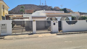 Uma área residencial murada com um edifício branco, uma montanha ao fundo e um céu claro.
