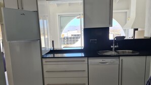 Cozinha moderna com armários brancos, bancada preta, lava-louças Bosch e janela com vista para edifícios e montanhas.