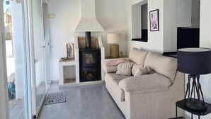 Uma sala de estar com um sofá bege, lareira, abajur e uma porta de vidro deslizante que dá para uma área externa.