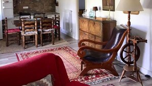 Uma sala de estar ampla com um sofá vermelho, uma cadeira de madeira, um espaço de refeições com mesa e cadeiras de madeira, e uma cozinha com painel de fundo de pedra.