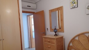Quarto com guarda-roupa de madeira, mesa de cabeceira com objeto decorativo, espelho e cama.