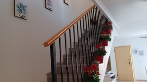 Uma escadaria com guarda-corpos pretos e balaústres de madeira, que leva a um patamar com plantas em vasos vermelhos.
