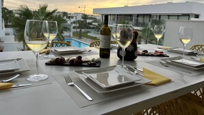 Mesa de jantar posta com taças de vinho, pratos e talheres, com vista para uma piscina e edifícios.