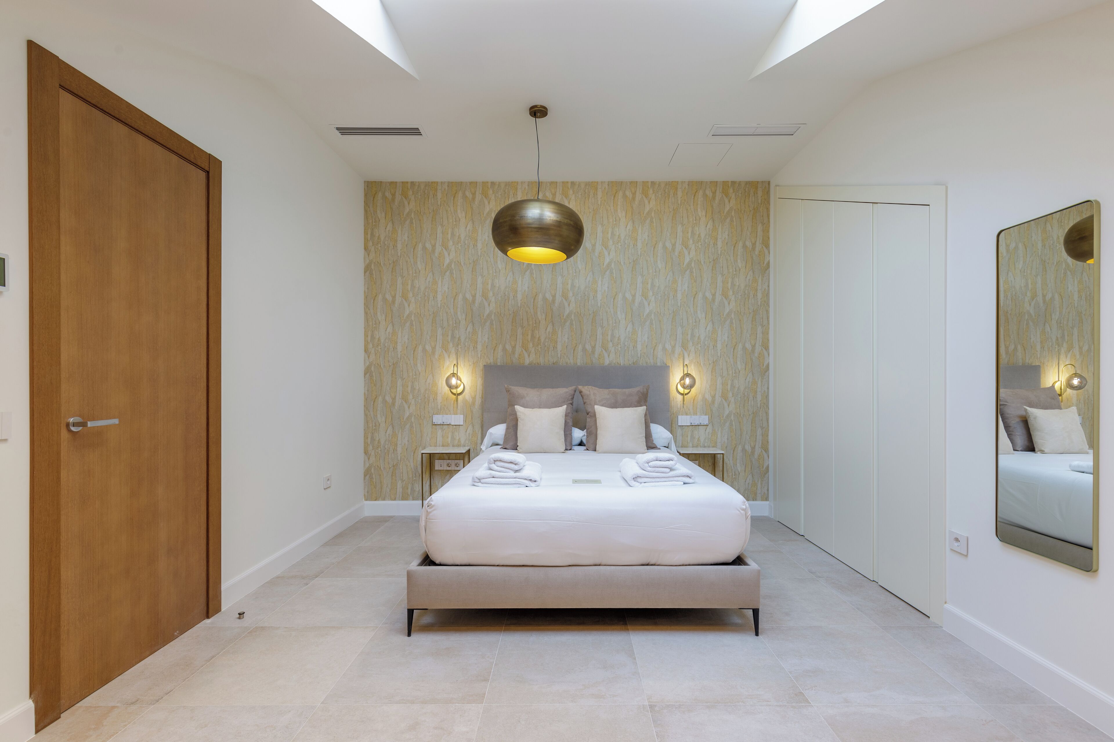 Quarto moderno com cama grande, claraboia e espelho fixado na parede.
