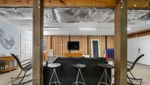 Um interior moderno com teto de madeira, sofá preto e banquetas de metal.