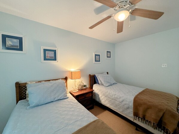 Quarto com duas camas, um ventilador de teto e quadros nas paredes.